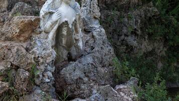 Escultura de pedra parcialmente incrustada em terreno rochoso, com vegetação ao redor.