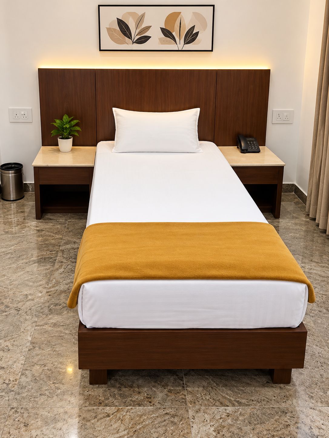 Quarto de hotel com uma cama, mesas de cabeceira, telefone, planta e uma obra de arte emoldurada na parede.