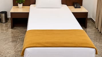 Quarto de hotel com uma cama, mesas de cabeceira, telefone, planta e uma obra de arte emoldurada na parede.