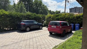 Dois carros estacionados em um caminho de paralelepípedos, com um hedge e árvores ao fundo.