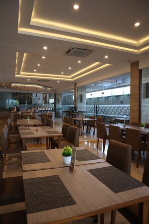 Restaurante moderno com várias mesas e cabines de refeição, área de cozinha ao fundo e uma grande janela que oferece luz natural.