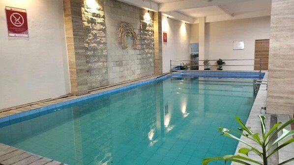 Piscina interna com parede de pedra, placa de segurança e porta de madeira.