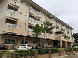 Edifício residencial de vários andares com varandas, aparelhos de ar condicionado e carros estacionados.