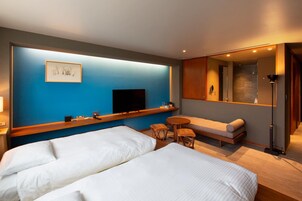 Quarto de hotel com duas camas, televisão, sofá, mesa pequena e espelho.