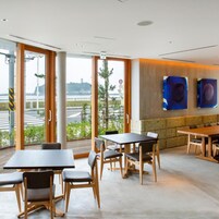 Interior moderno de restaurante com grandes janelas, mesas e cadeiras de madeira.