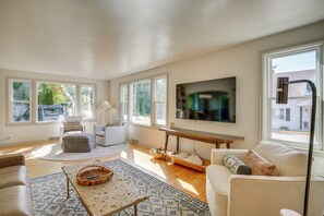 Uma sala de estar ampla com uma grande TV de tela plana na parede, uma área de estar aconchegante com sofá e poltronas, e uma mesa de centro de madeira.