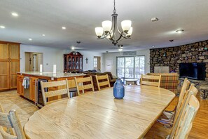 Uma sala de jantar espaçosa com mesa e cadeiras de madeira, um candelabro e uma parede de pedra com televisão.