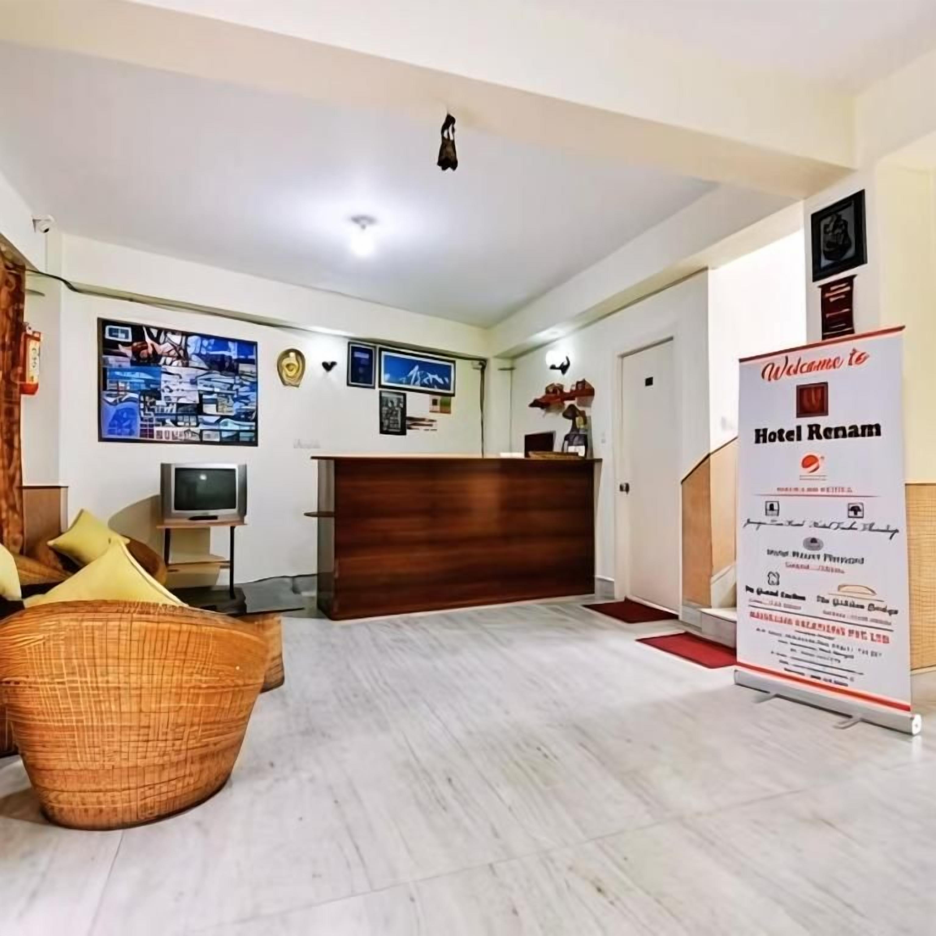 Uma área de recepção de hotel, com balcão, televisão e placa de boas-vindas.