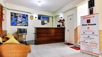 Uma área de recepção de hotel, com balcão, televisão e placa de boas-vindas.