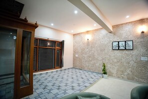 Quarto com piso estampado, janela com persianas, luminária fixada na parede e quadro decorativo.