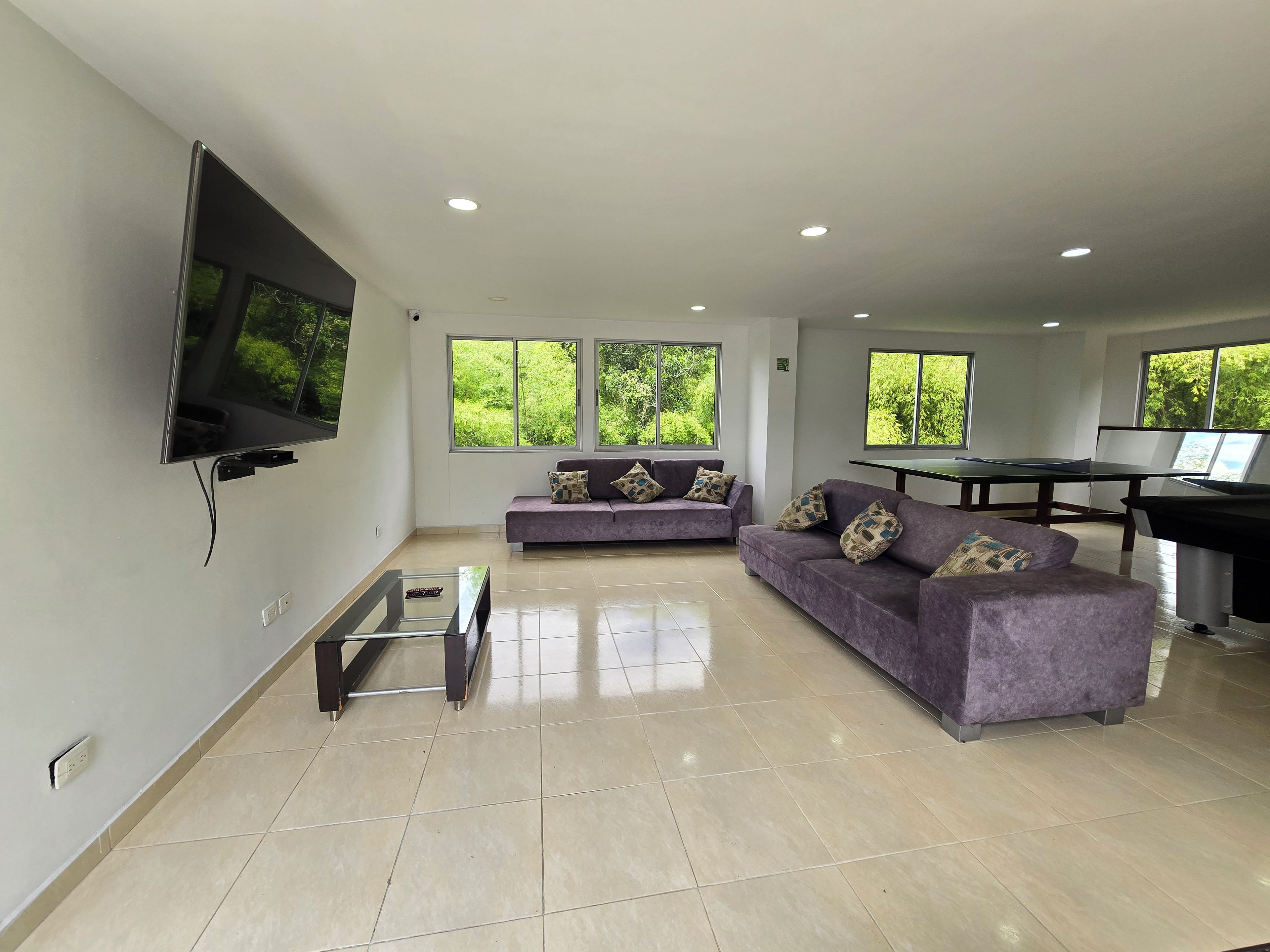 Uma sala de estar moderna com televisão de tela plana, dois sofás, uma mesa de centro e uma mesa de pingue-pongue.