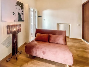 Quarto com cama, luminária de chão, radiador e porta para outro cômodo.