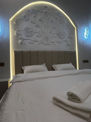 Quarto de hotel com cama, almofadas e cabeceira decorada com flores.