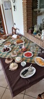 Mesa de jantar posta com diversos pratos, utensílios e lareira de tijolos.
