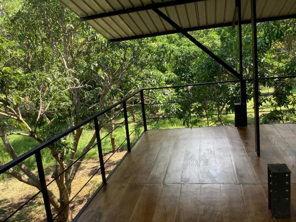 Um deck de madeira ao ar livre com guarda-corpo de metal, cercado por árvores.