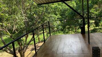 Um deck de madeira ao ar livre com guarda-corpo de metal, cercado por árvores.