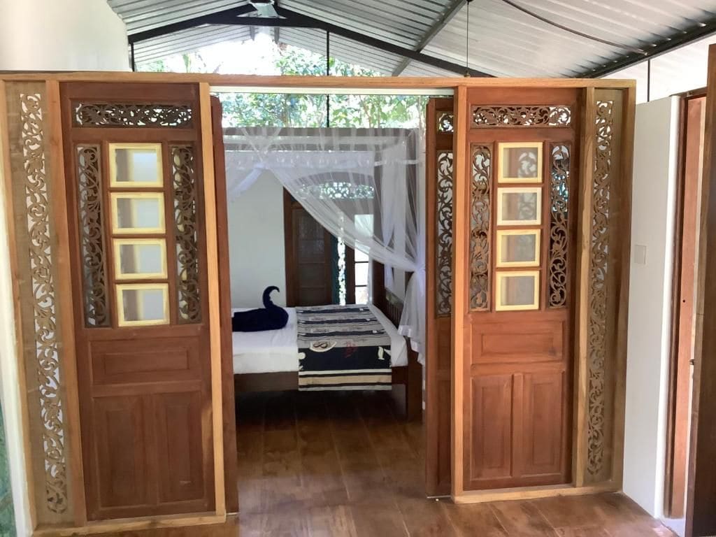 Quarto com cama, um banco e porta de madeira decorativa com detalhes elaborados.