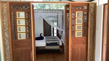 Quarto com cama, um banco e porta de madeira decorativa com detalhes elaborados.