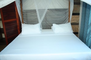Uma cama com dossel, roupa de cama branca e cabeceira encostada a uma parede de pedra.