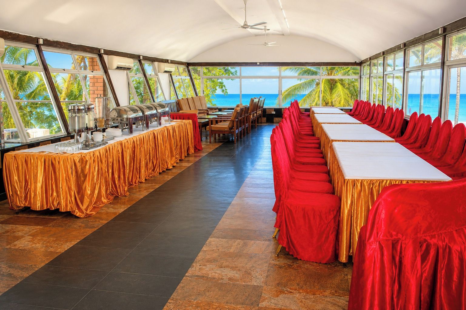 Restaurante com vista para o oceano, com mesas e cadeiras compridas e um ventilador de teto.