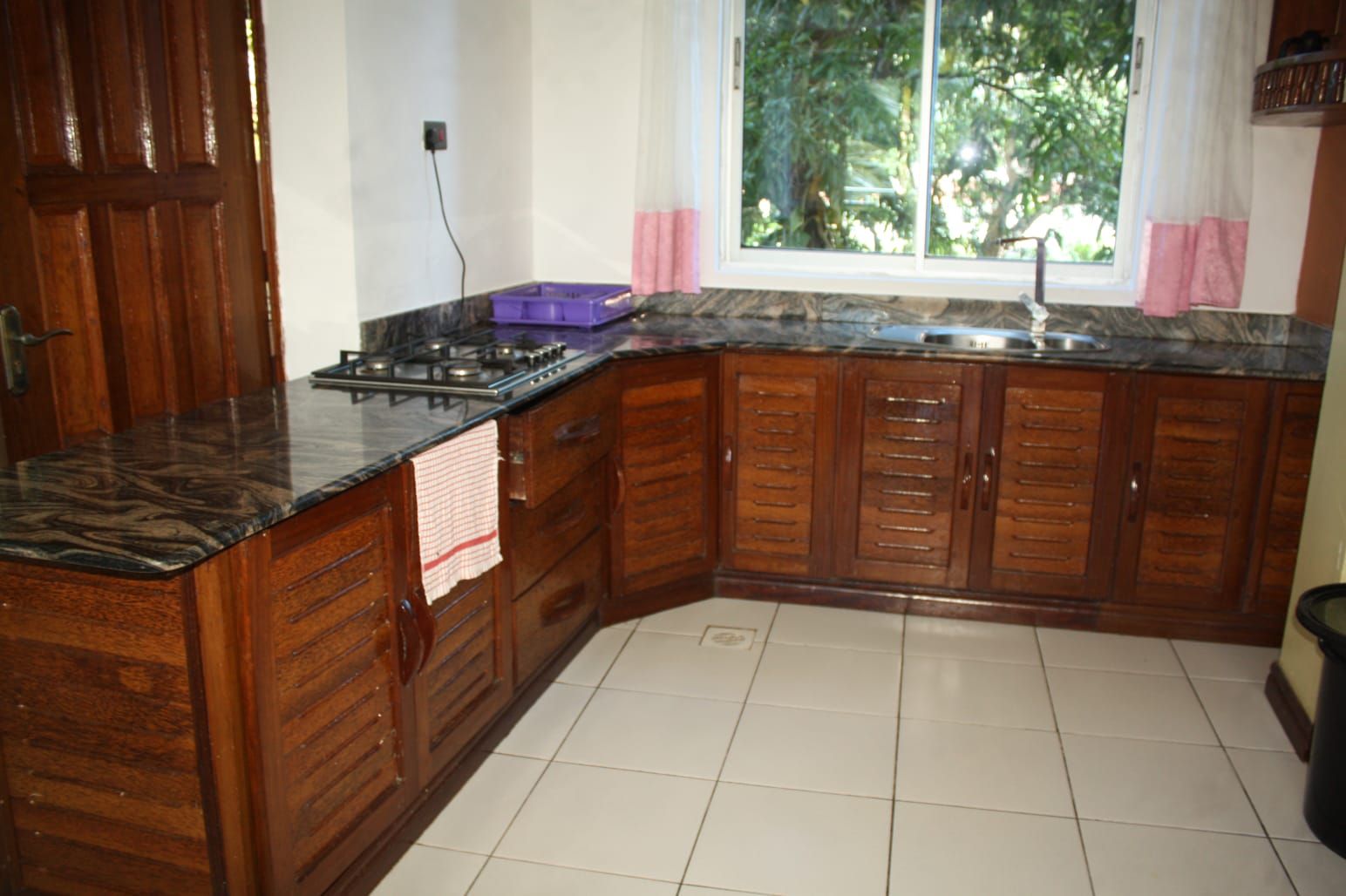 Cozinha com armários de madeira, bancada de granito e janela com cortinas.