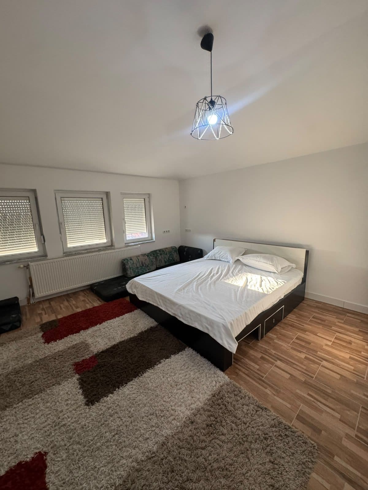 Quarto com cama, radiador, janela e luminária no teto.
