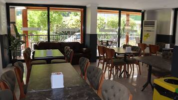 Um restaurante com mesas internas, janelas amplas e vista para o exterior.