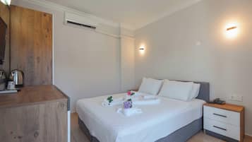 Quarto de hotel com cama, mesa de cabeceira e escrivaninha de madeira com chaleira.