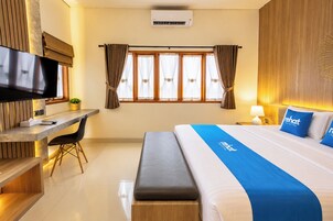 Quarto de hotel com cama, escrivaninha, cadeira, televisão e janela com cortinas.