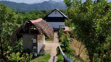 Uma trilha leva a uma construção com telhado de palha e a um edifício moderno com telhado inclinado.