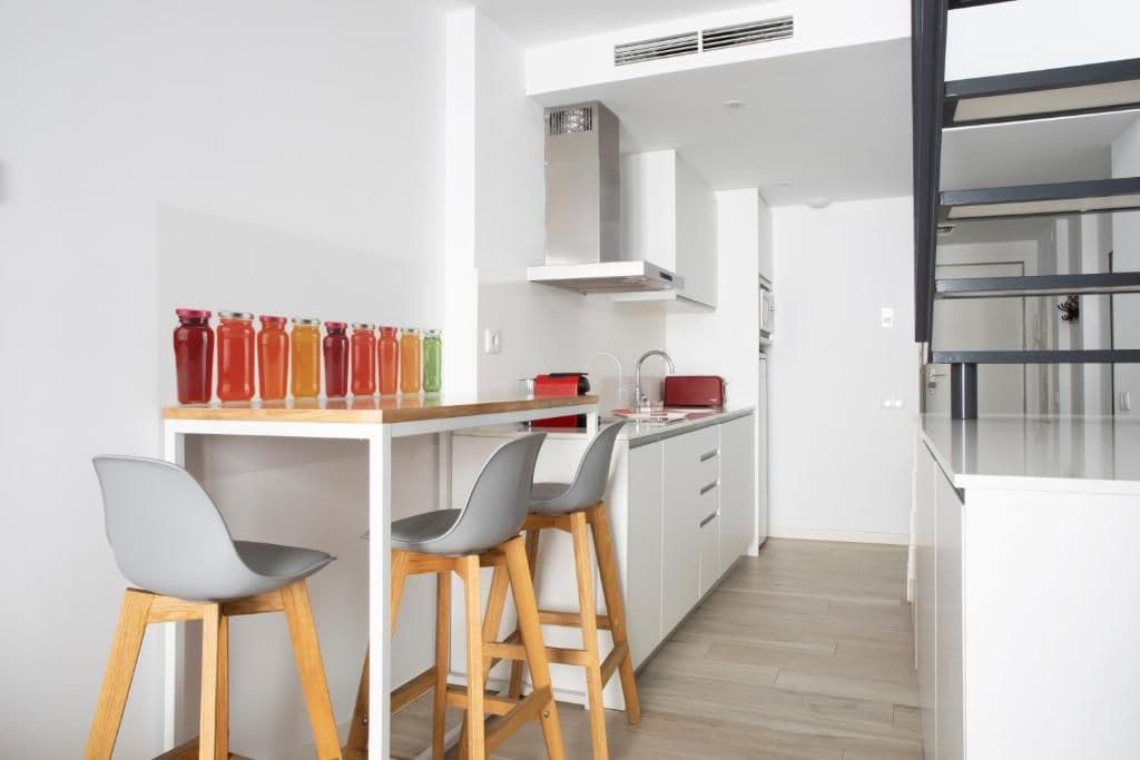 Cozinha moderna com armários brancos, exaustor de aço inoxidável e área de bar com banquetas.