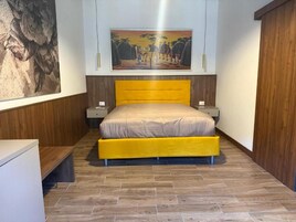 Quarto com cama, mesas de cabeceira, cabeceira de madeira, quadro sobre a cama e guarda-roupa.