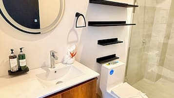 Casa de banho moderna com espelho redondo, lavatório branco, sanita e cabine de duche com parede de vidro.