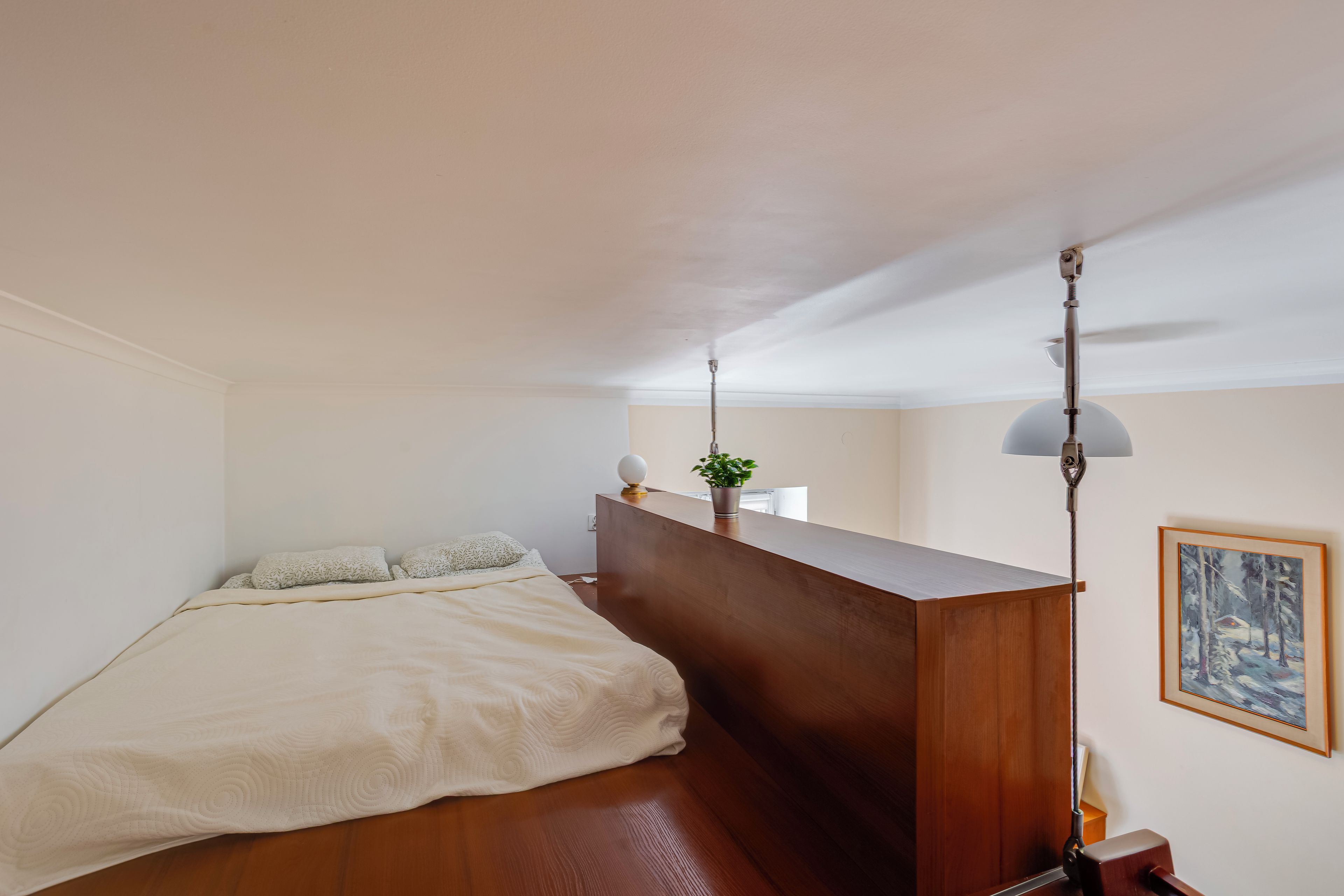 Quarto com cama, escrivaninha de madeira, luminária e pintura na parede.