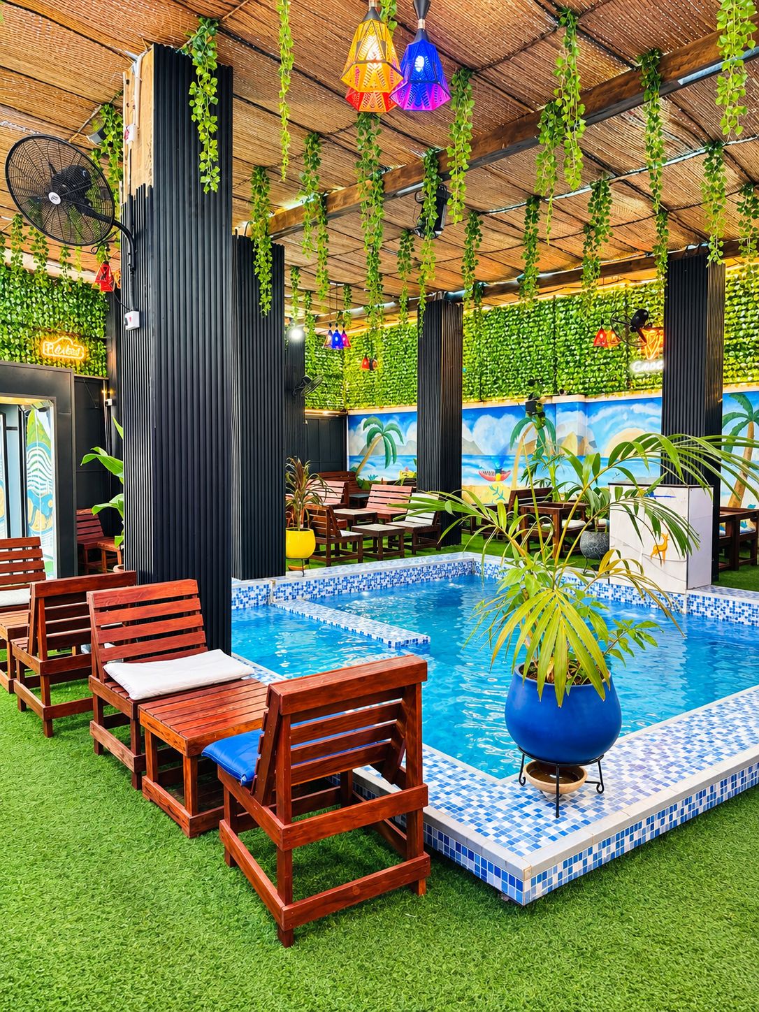 Área de piscina com cadeiras de madeira e piscina azulejada em azul.