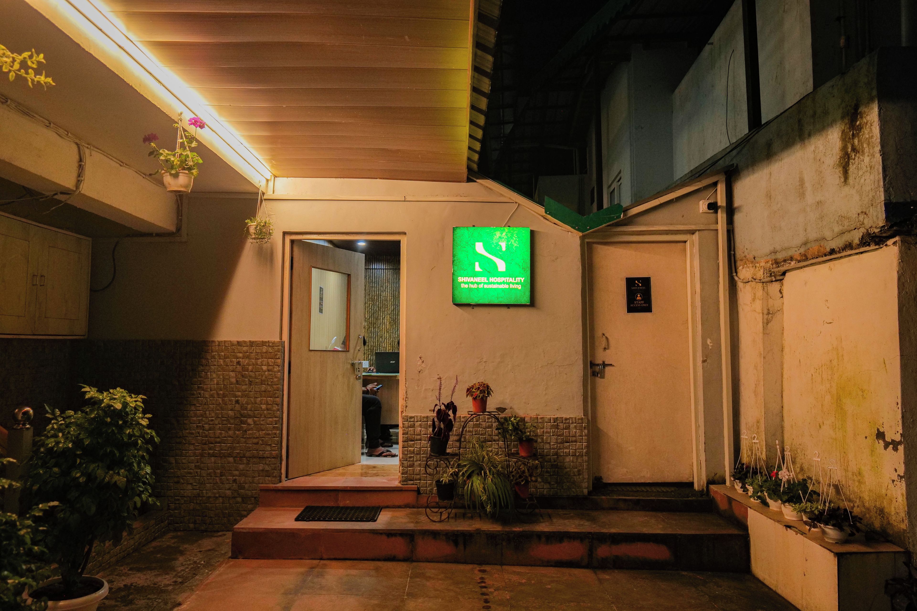 Entrada de hotel com um letreiro verde, escada e plantas em vasos.