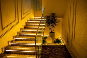 Escadaria com corrimão de vidro, planta em vaso e pequena área de jardim com pedriscos e plantas.