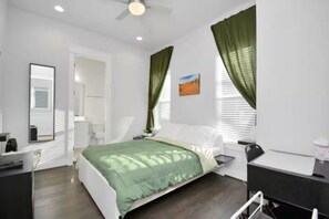 Quarto com cama, escrivaninha, cadeira, espelho e janela com cortinas.