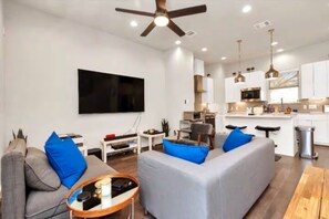 Uma sala de estar moderna com um sofá cinzento, almofadas azuis, uma mesa de centro e uma televisão de ecrã plano na parede.