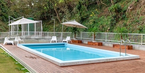 Piscina retangular com deck de madeira, rodeada por grades brancas e plantas em vasos.