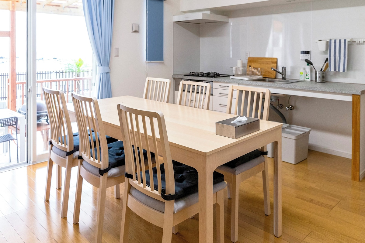 Cozinha moderna com área de refeições, cadeiras de madeira e vista para o exterior.