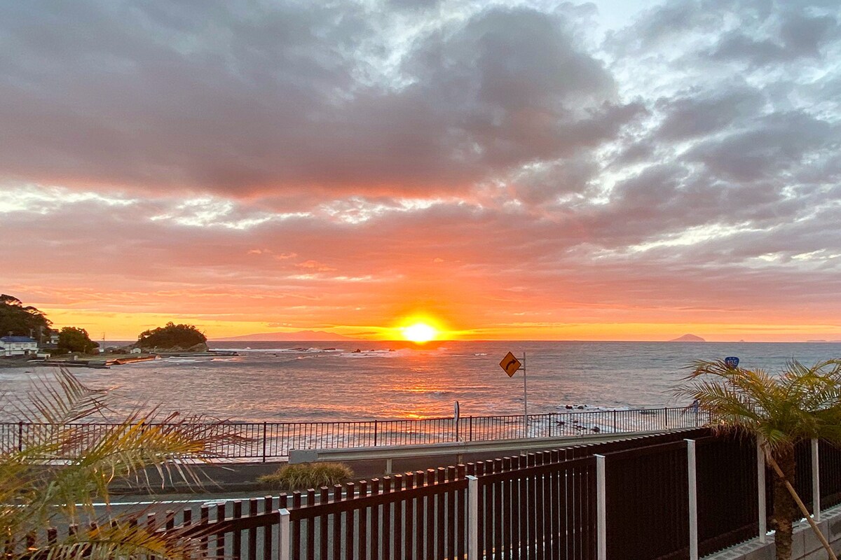 Pôr do sol sobre a água, com uma estrada e uma cerca ao primeiro plano.