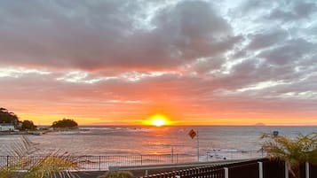 Pôr do sol sobre a água, com uma estrada e uma cerca ao primeiro plano.