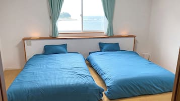 Quarto com duas camas de solteiro, janela com cortinas e vista para o mar.
