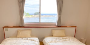 Quarto com duas camas, janela com cortinas e vista para o mar.