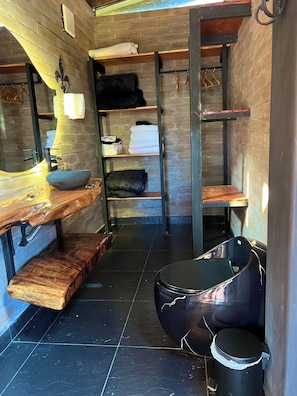 Casa de banho compacta com toucador de madeira, lavatório preto e um contentor de lixo preto.