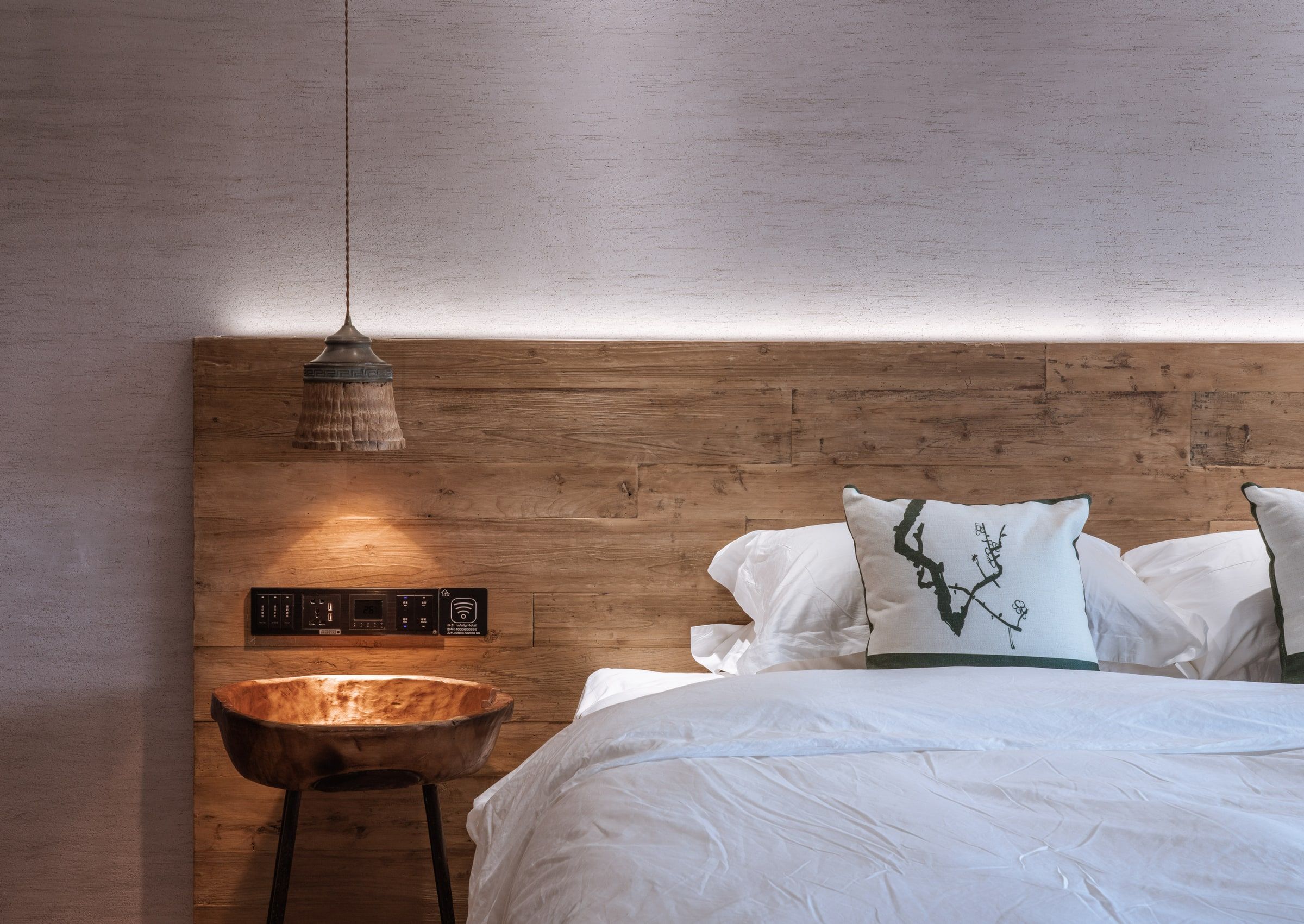 Quarto com cabeceira de madeira, mesa de cabeceira com abajur e cama com almofadas.