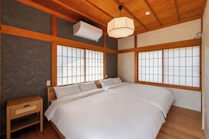 Quarto tradicional japonês com cama grande, vigas de madeira, portas deslizantes shoji e ventoinha de teto.