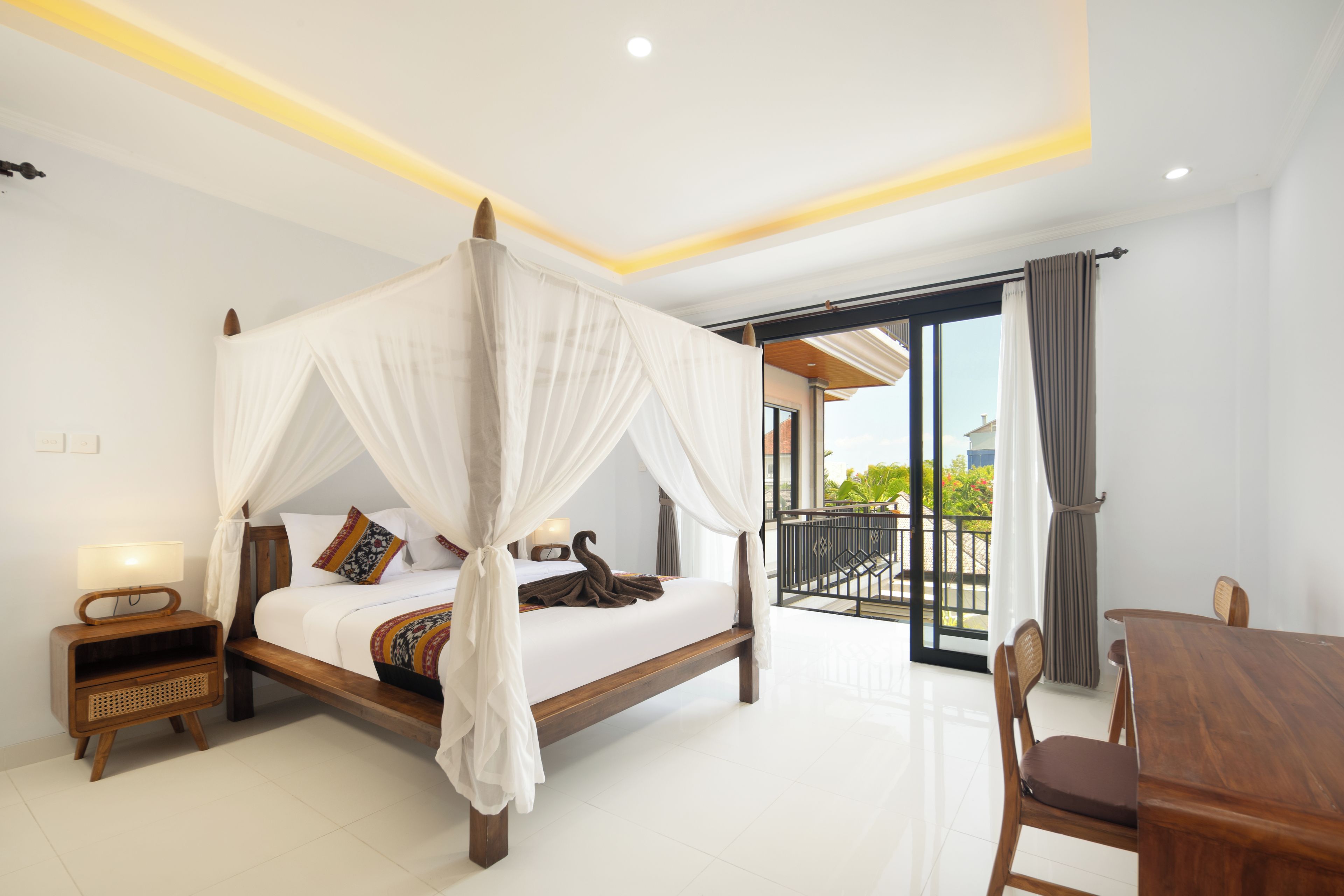 Quarto com cama de dossel, mesa de cabeceira, abajur, mesa de jantar com cadeiras e vista para o exterior.