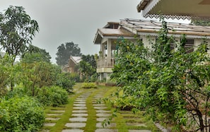 Caminho que leva a um edifício com varanda, cercado por vegetação exuberante.